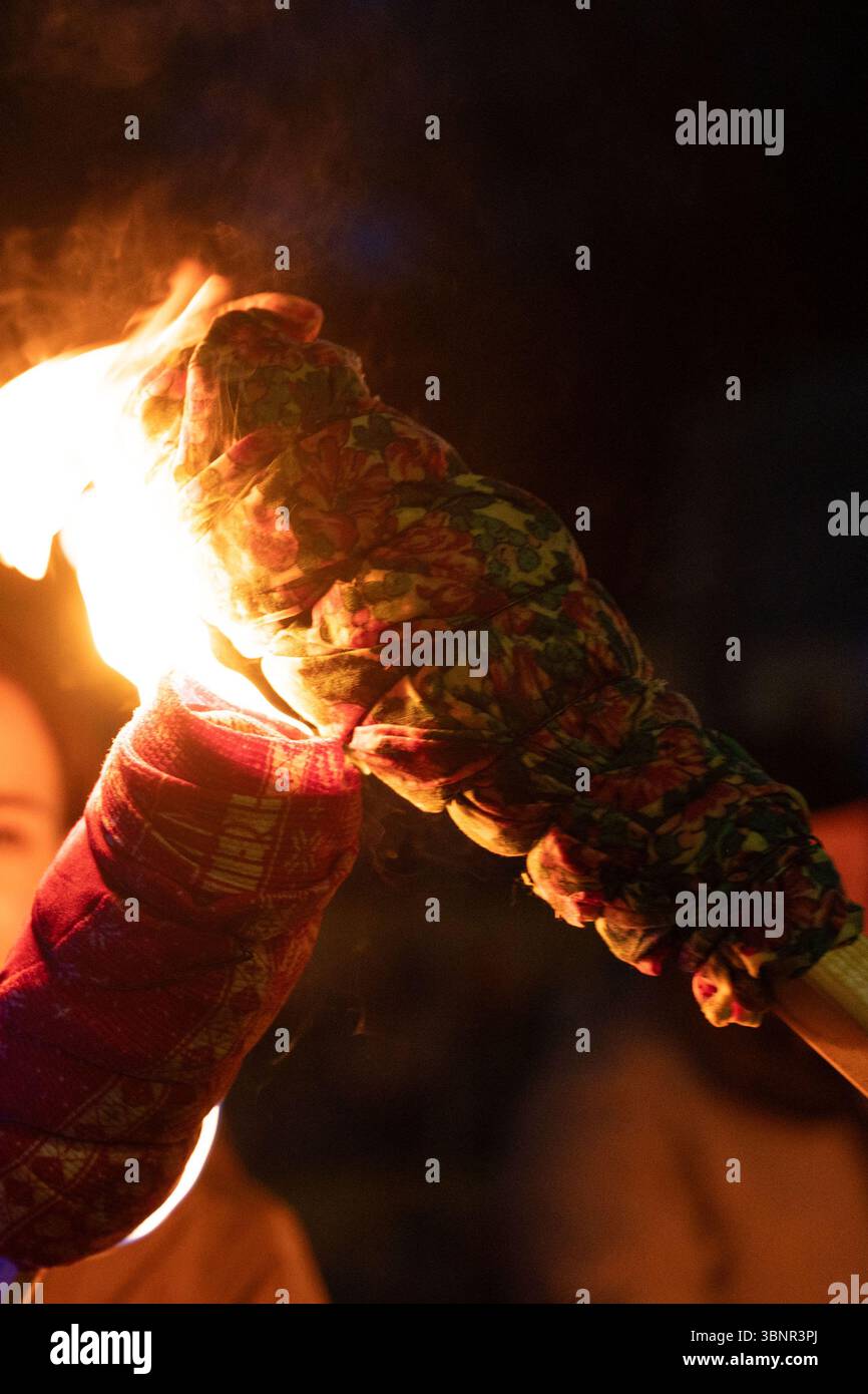 Close-up of a flaming torch held by someone at night. A person's face ...