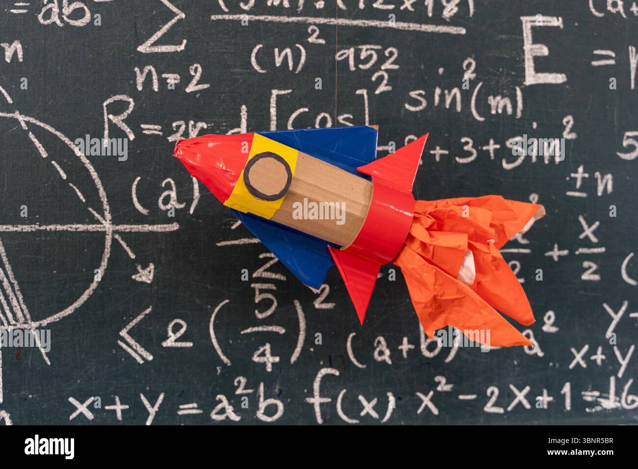 Handmade paper rocket model in front of chalkboard with mathematical ...