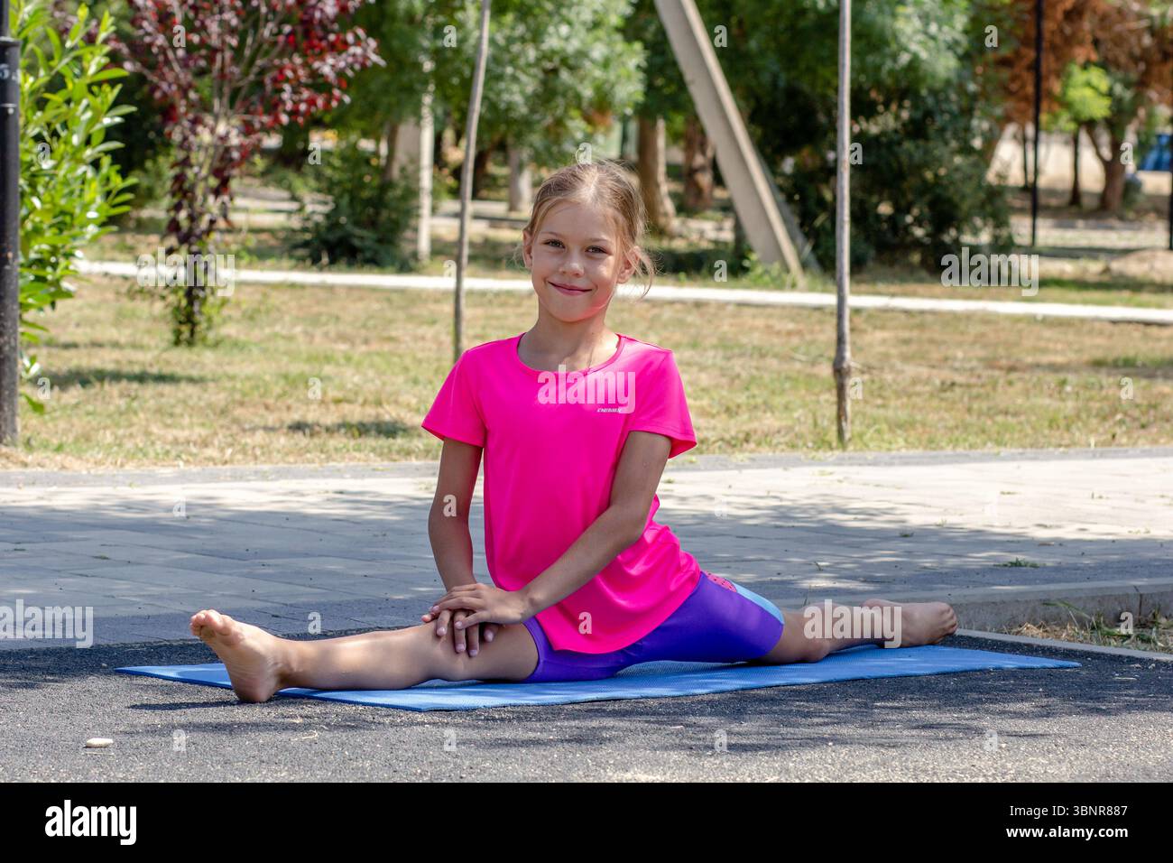 A child sitting on the pavement with legs extended straight forward and ...