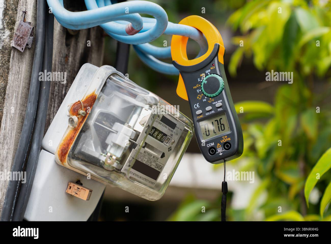 Digital clamp meter clamped on electric wire showing voltage reading on ...