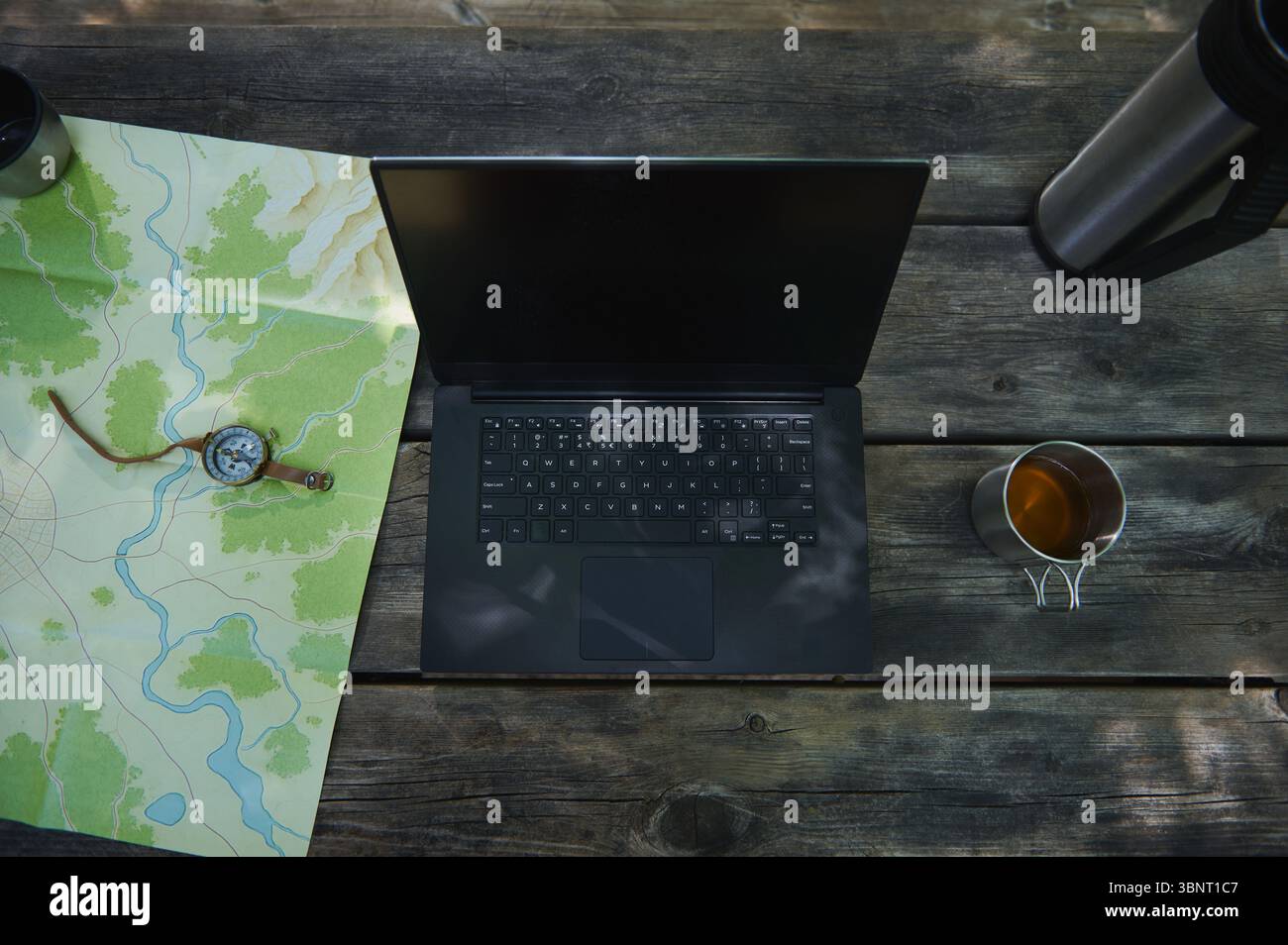 Desk setup with a laptop, a map, a compass, a metal mug of tea, and a ...