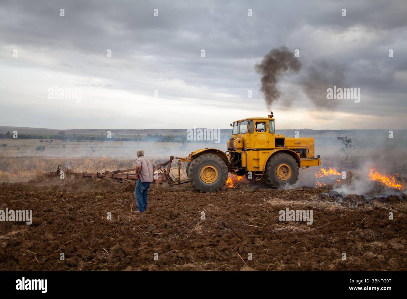 Farmer Operating Yellow Tractor Near Field Fire Under Stormy Sky Stock ...