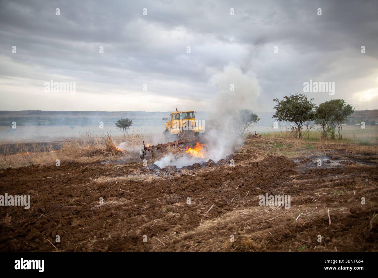 Yellow Tractor Near Field Fire Under Stormy Sky Stock Photo - Alamy