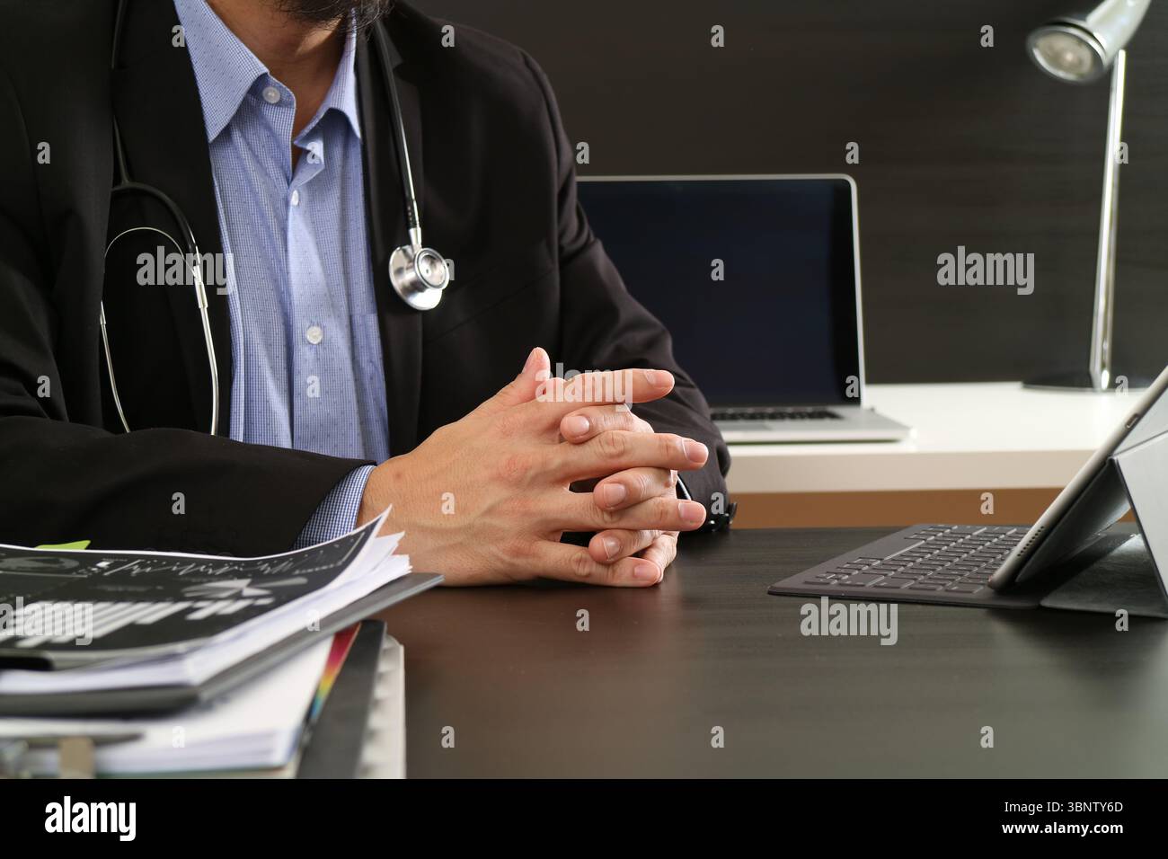 A doctor in a formal suit with a stethoscope around the neck sits at a ...