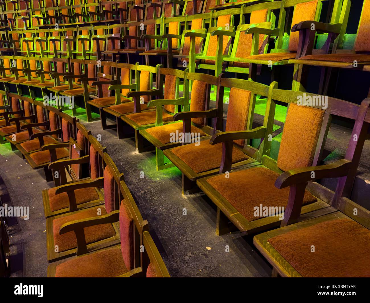 Rows of empty vintage wooden seats in a curved auditorium with colored ...