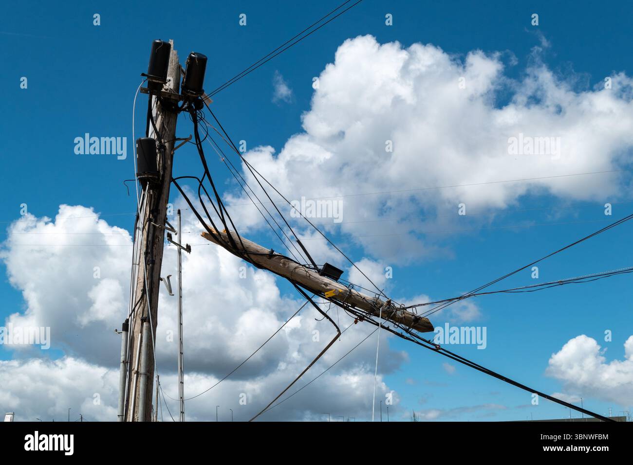 Broken telephone and fiber optic pole with suspended cables under a ...