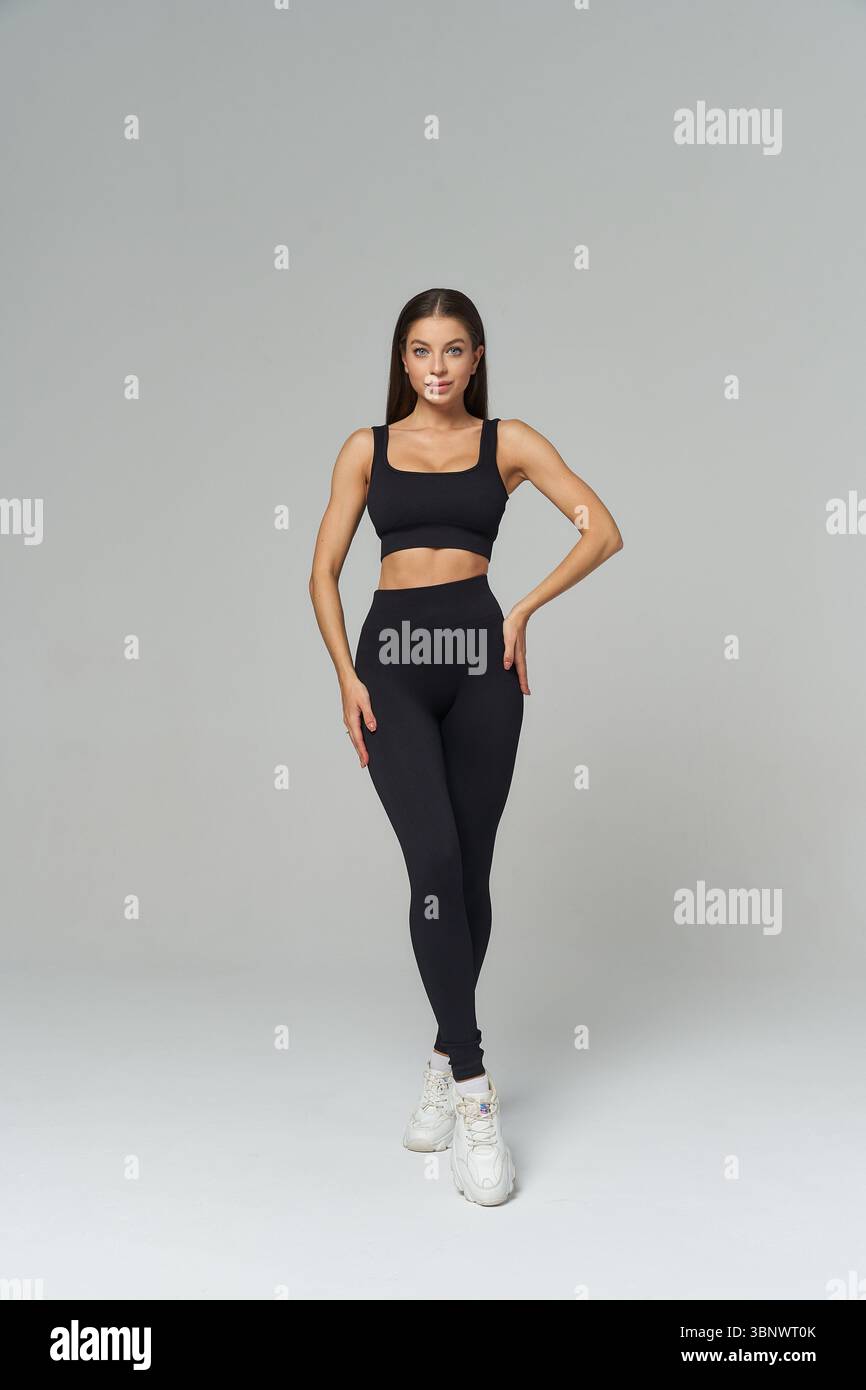 A woman with long hair stands confidently in black sportswear and white ...