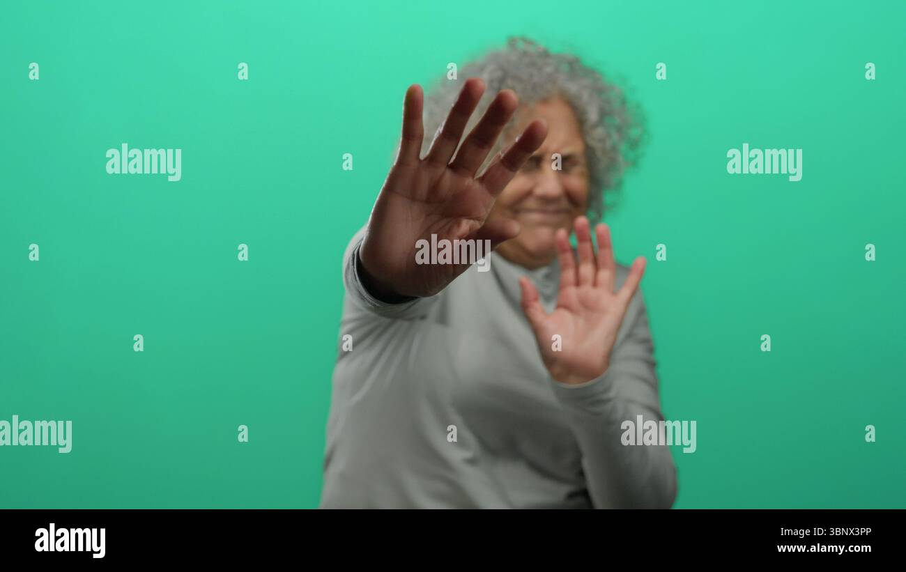 Woman expressing fear with hands raised against a green background ...