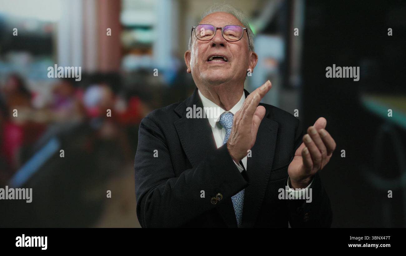 Senior man in a suit clapping joyfully at an outdoor restaurant terrace ...