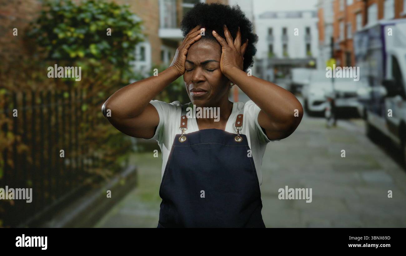 Woman in apron stands on city street, appearing stressed, hands on head ...