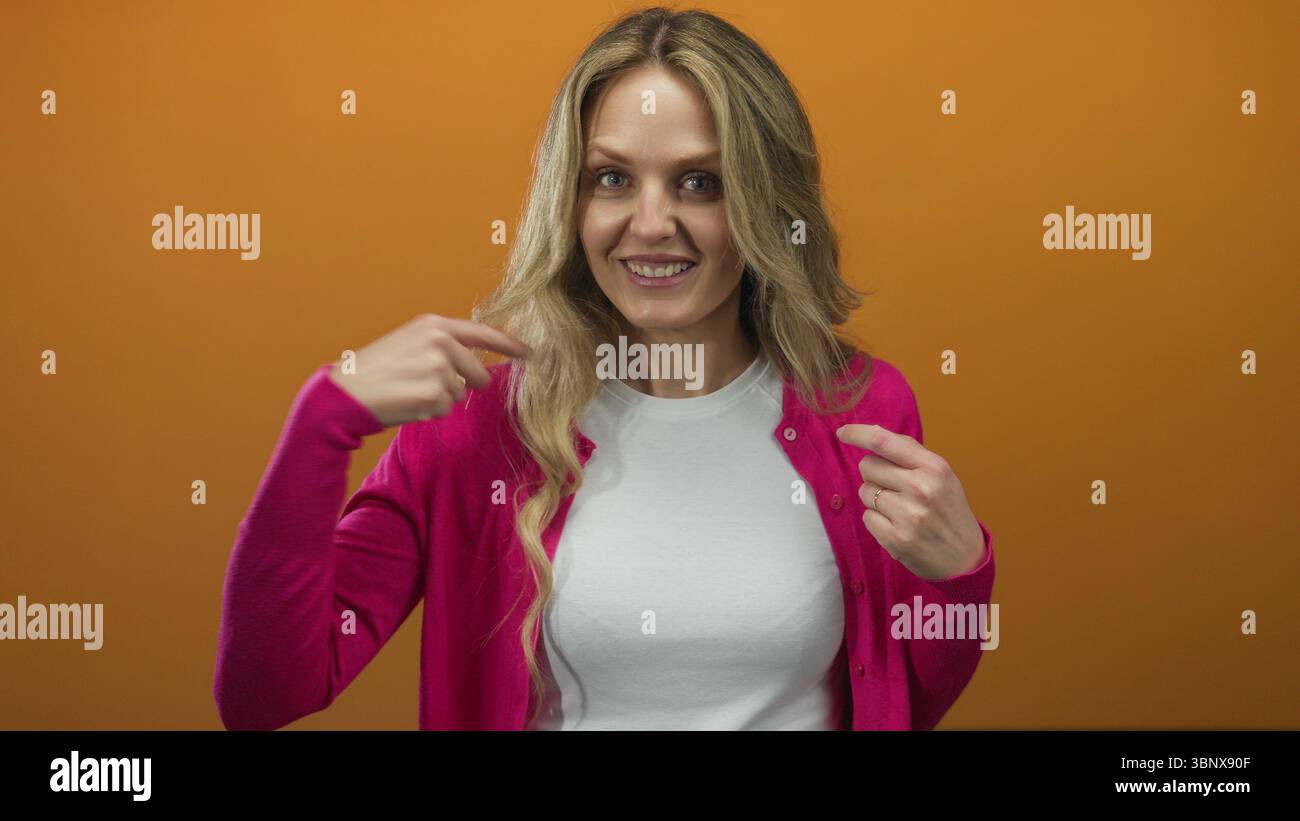 Woman pointing at herself with a playful smile in a pink cardigan ...