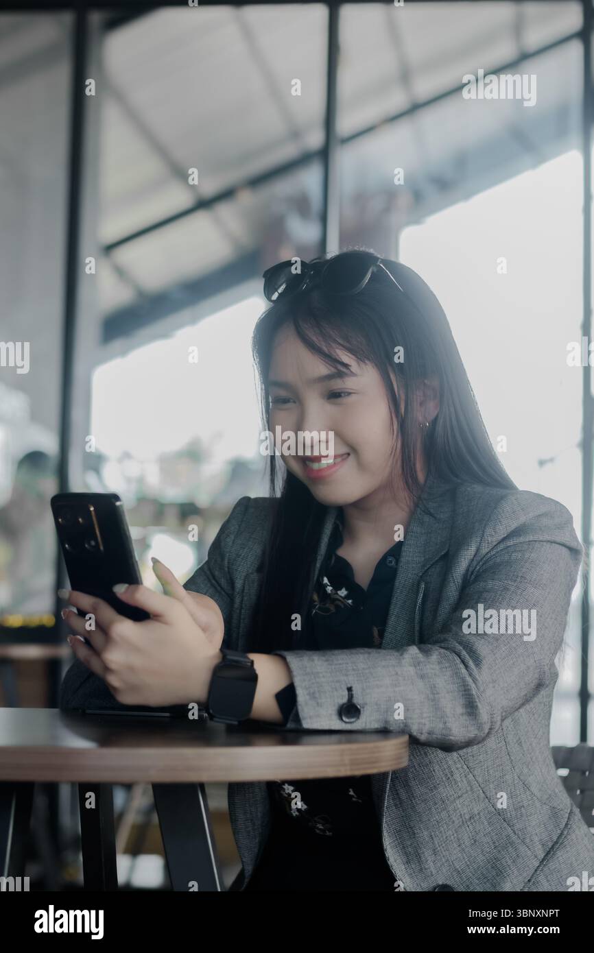 A beautiful asian woman in a blazer smiles as she checks her smartphone ...