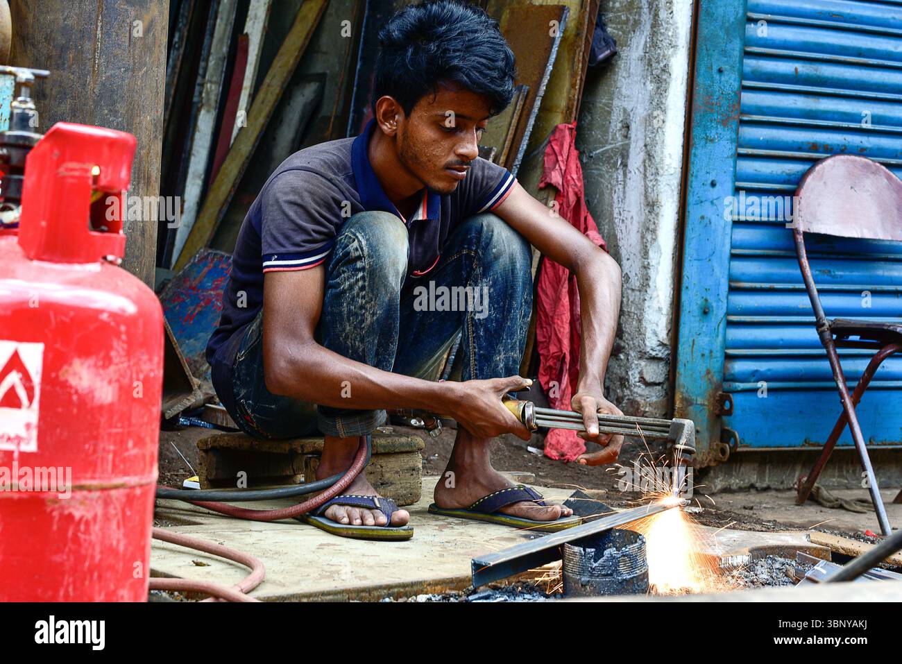 A young man sits on the ground in a workshop, carefully using a torch ...