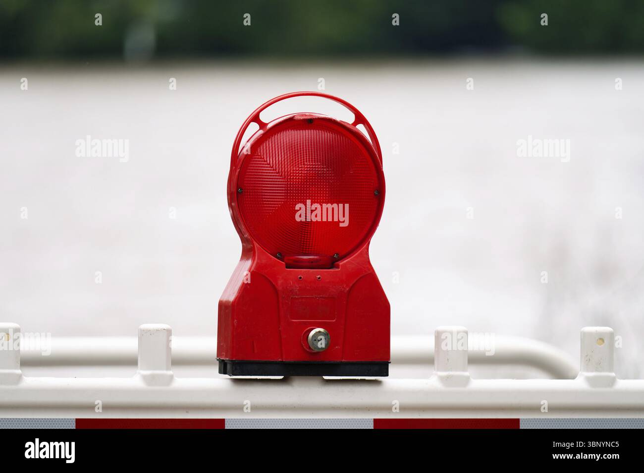 Red warning light on a barrier fence with flooded water surface in a ...