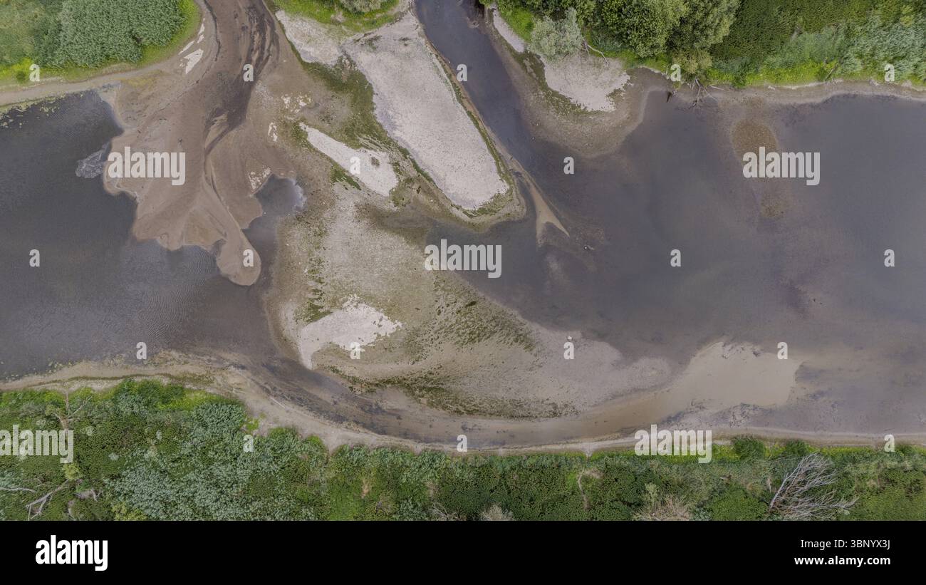 The picture shows a dry riverbed with exposed sand and silt, surrounded ...