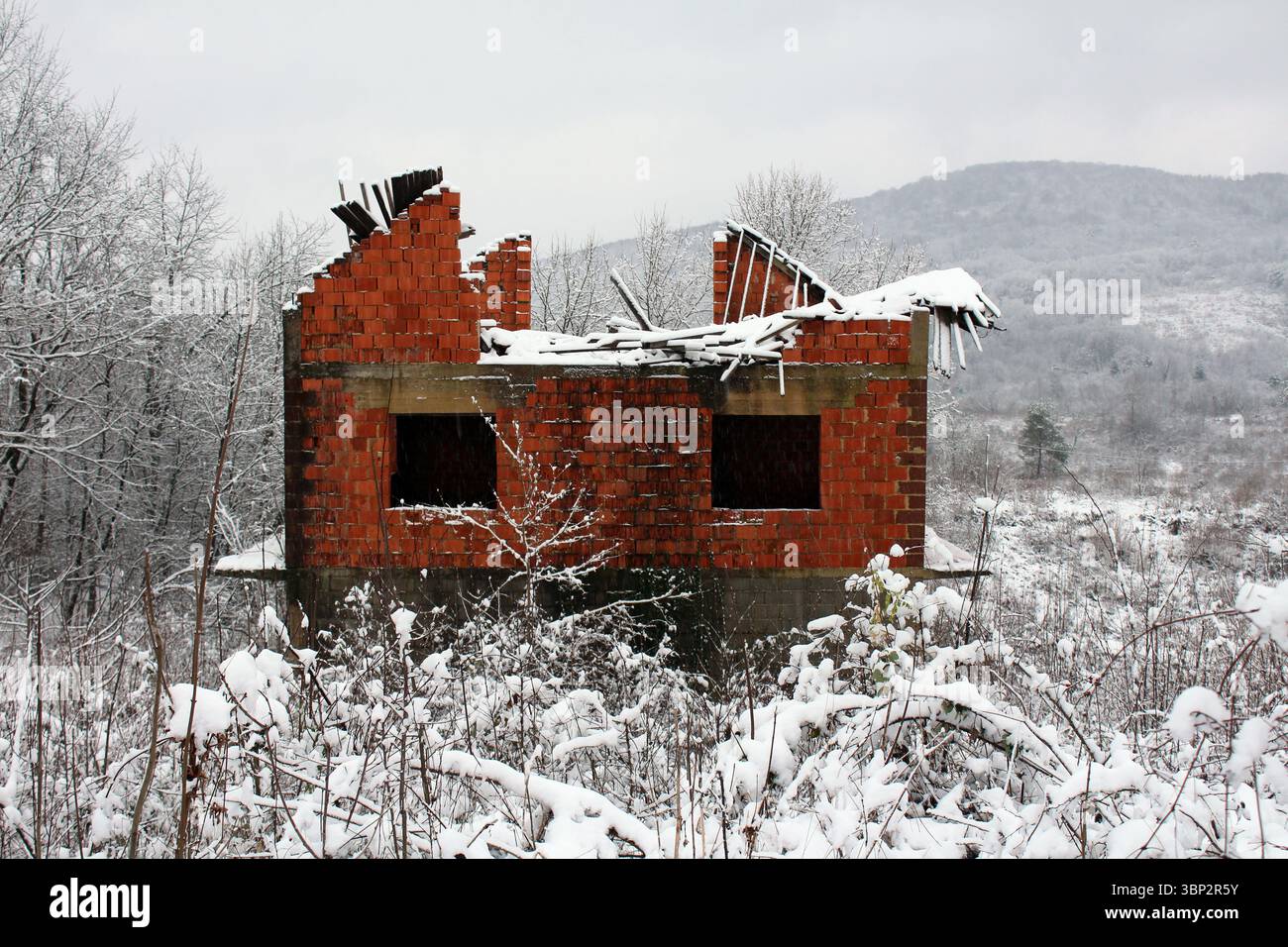 A partially collapsed red brick house stands deserted in a snow-covered ...