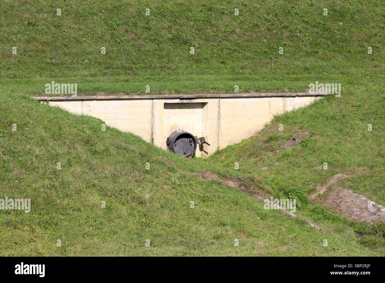 A concrete drainage culvert with a round metal cover is embedded in a ...