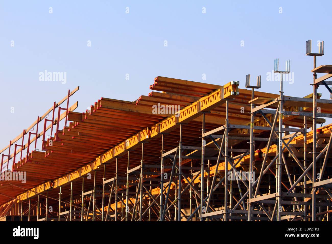 A network of metal scaffolding supports bright yellow wooden beams ...