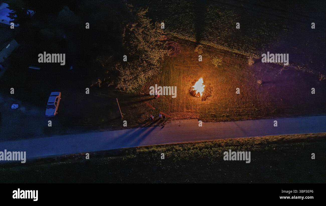 A group of people gather around a campfire in an open field at night ...