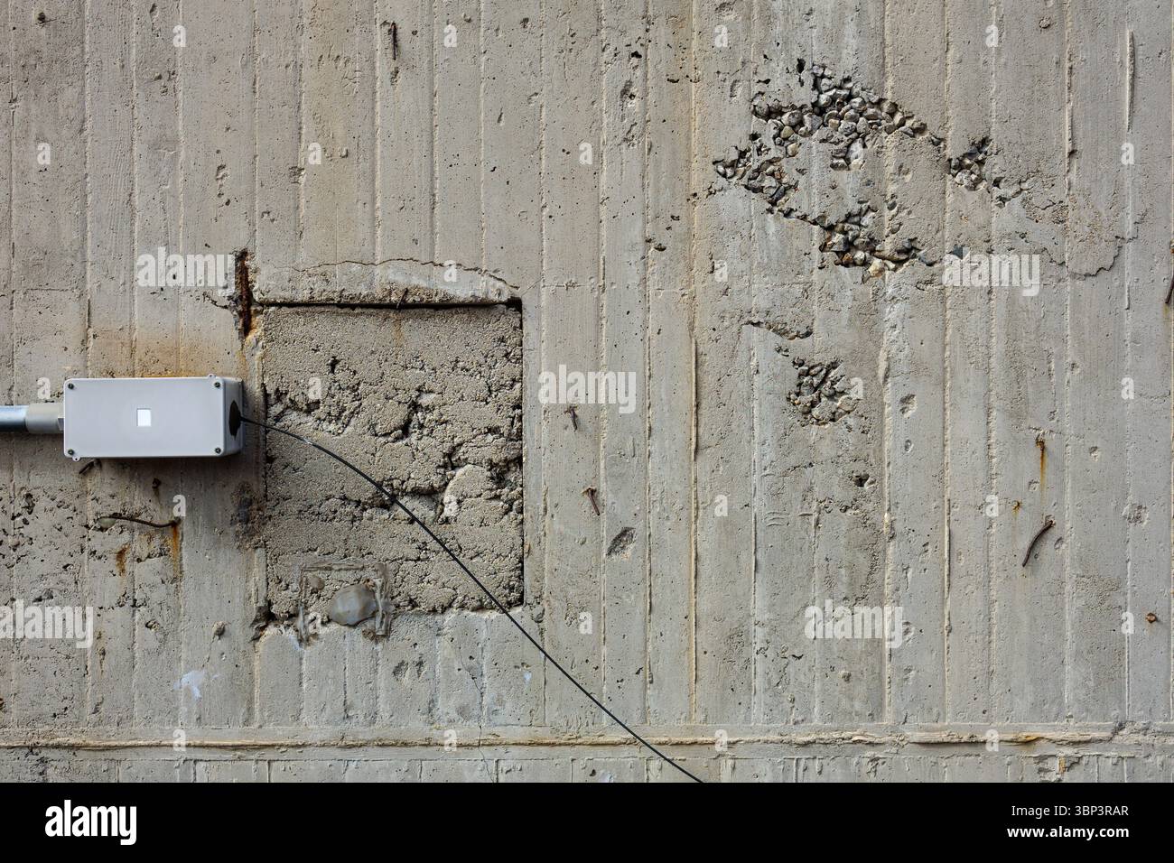 Weathered concrete wall features rectangular patch with exposed rebar ...