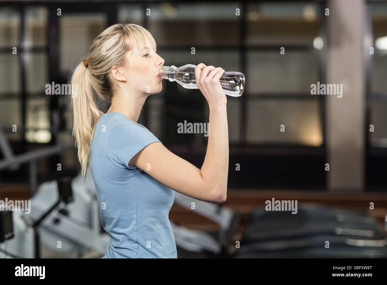 Female gym-goer drinking water from reusable bottle by treadmills in ...