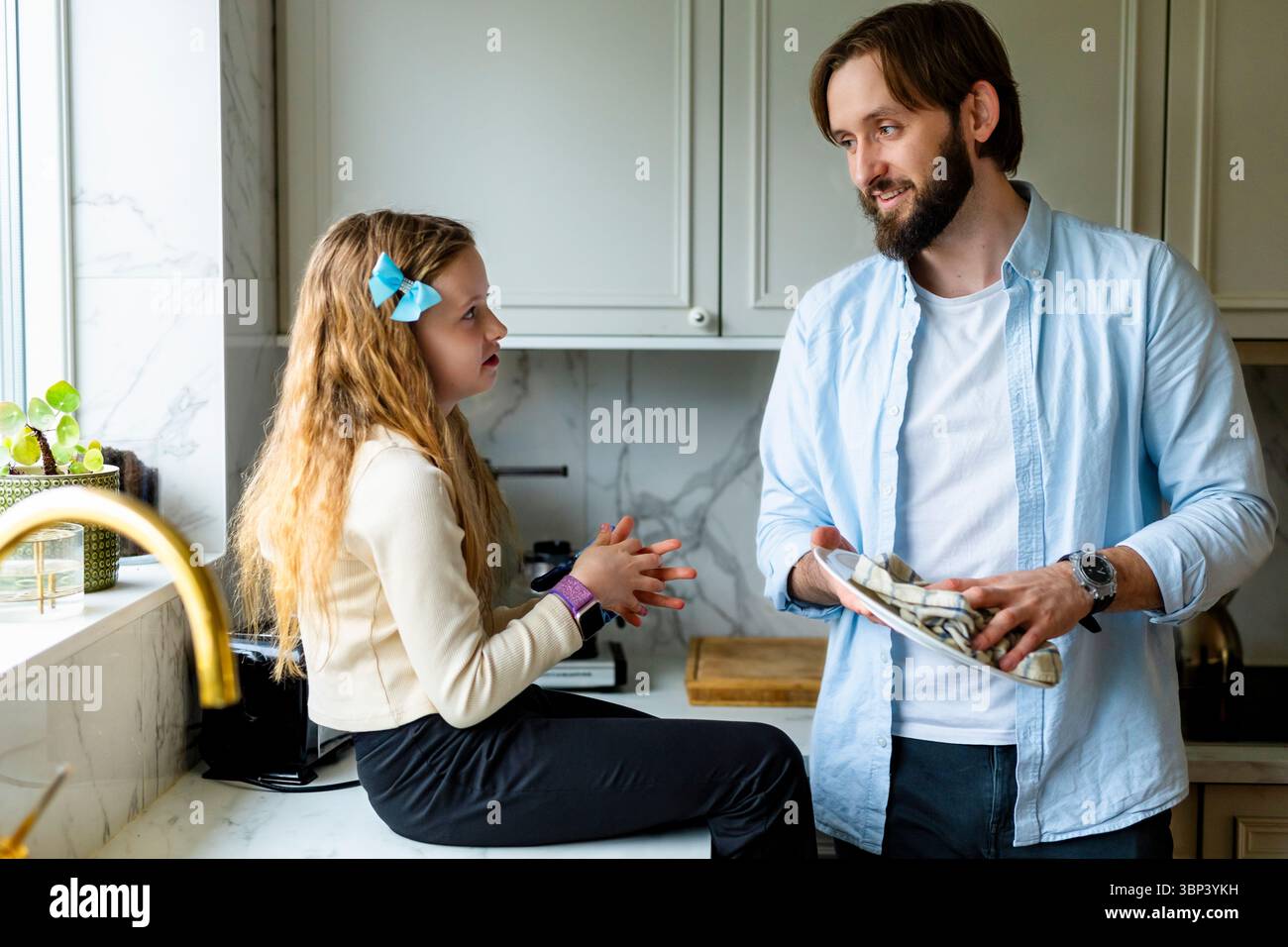 Father cleaning dishes while talking with daughter sitting on kitchen ...