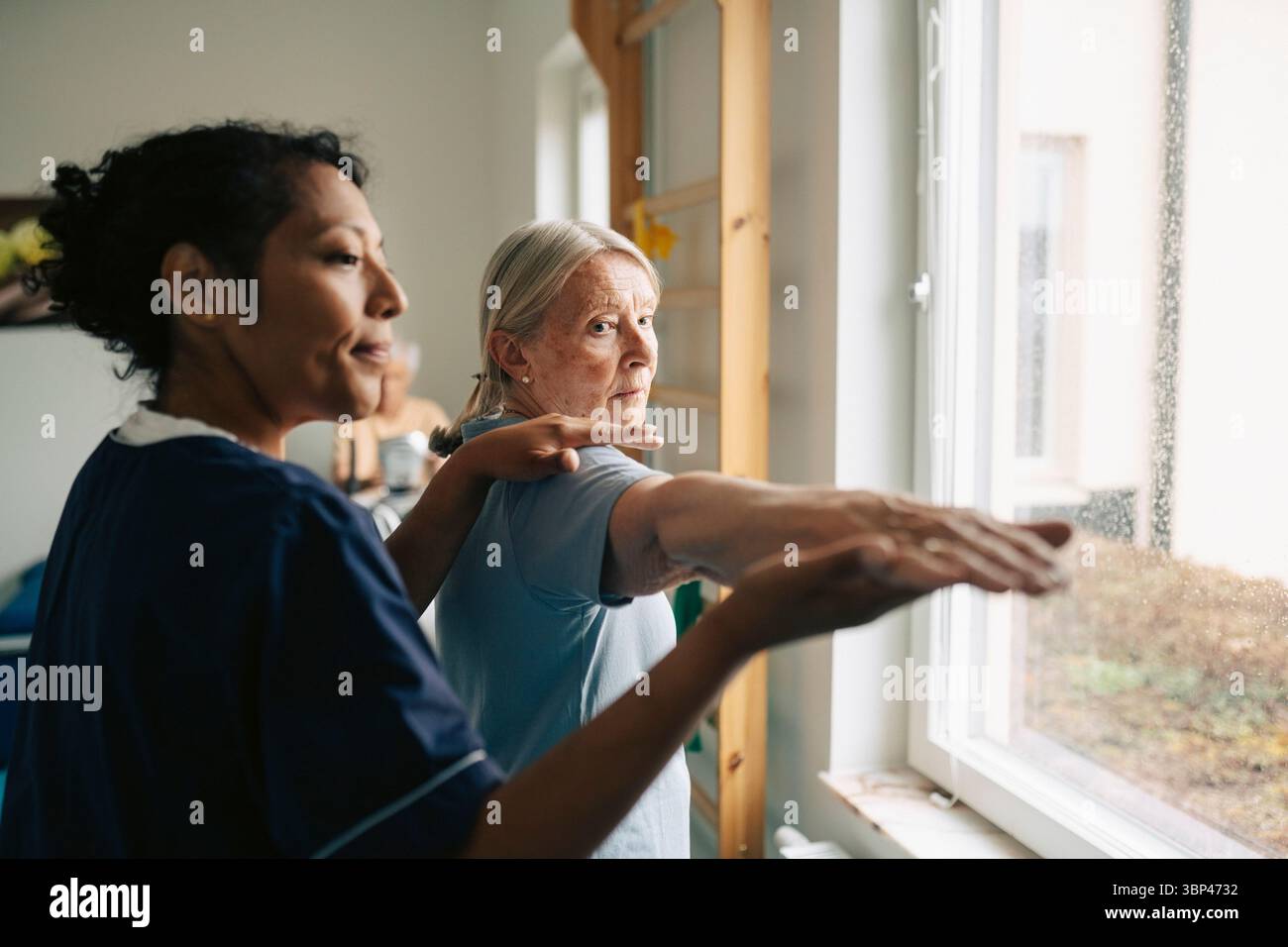 Female therapist helping senior woman with stretching exercise at ...