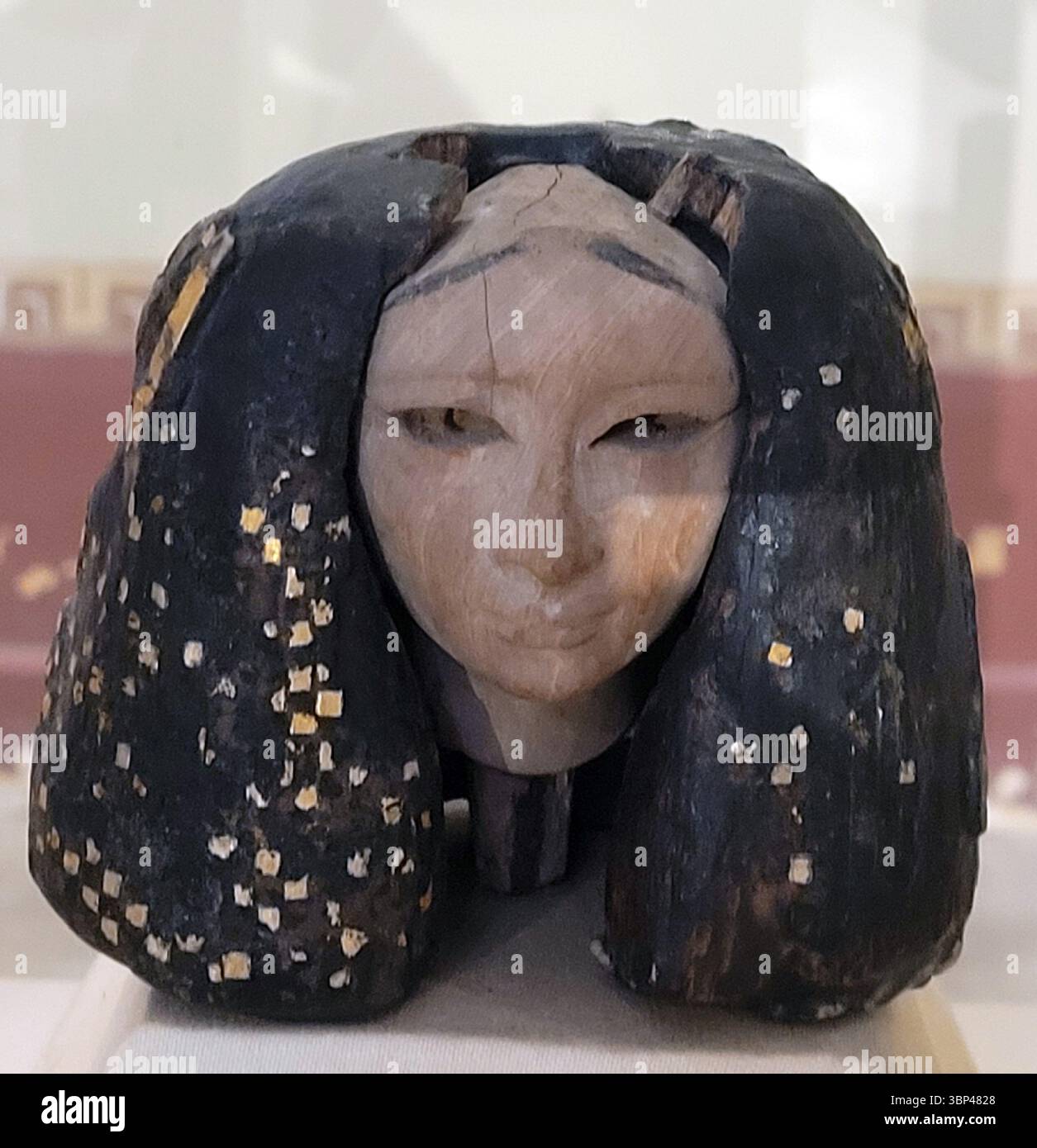 A photograph of the head of a female statue, made from painted wood and ...
