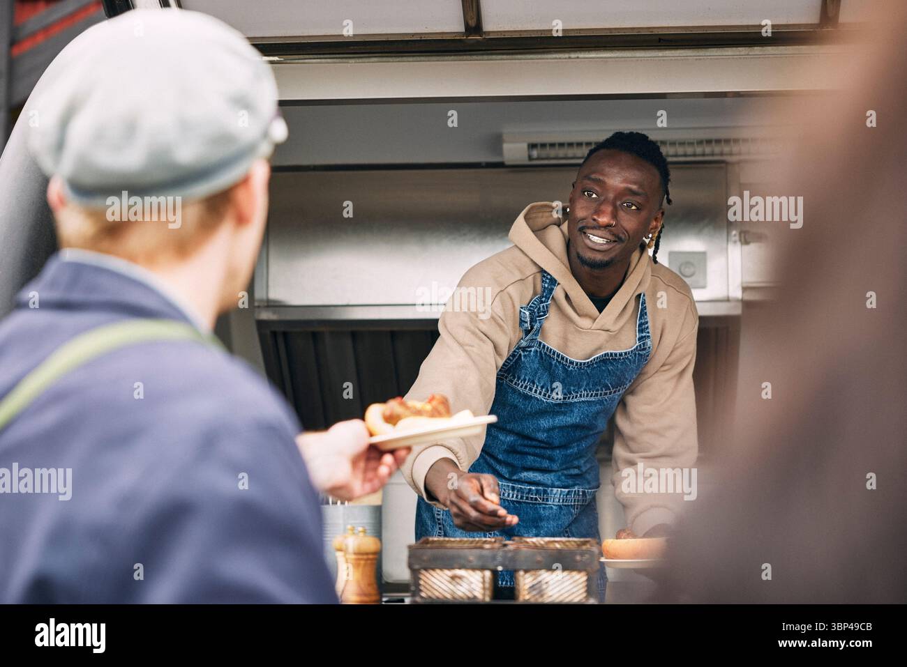 Young man wearing apron serving hot dog to customer while standing in ...