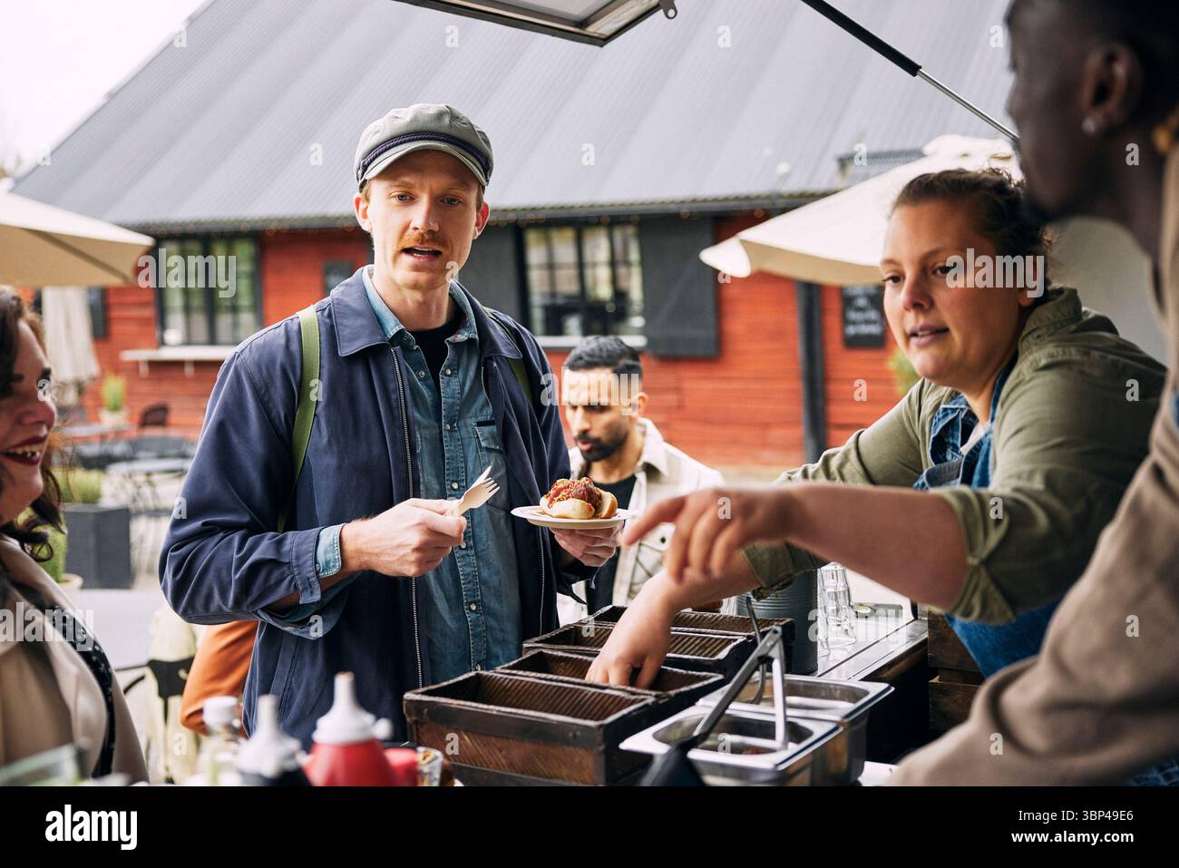 Man wearing cap holding hot dog plate while talking with owner at food ...