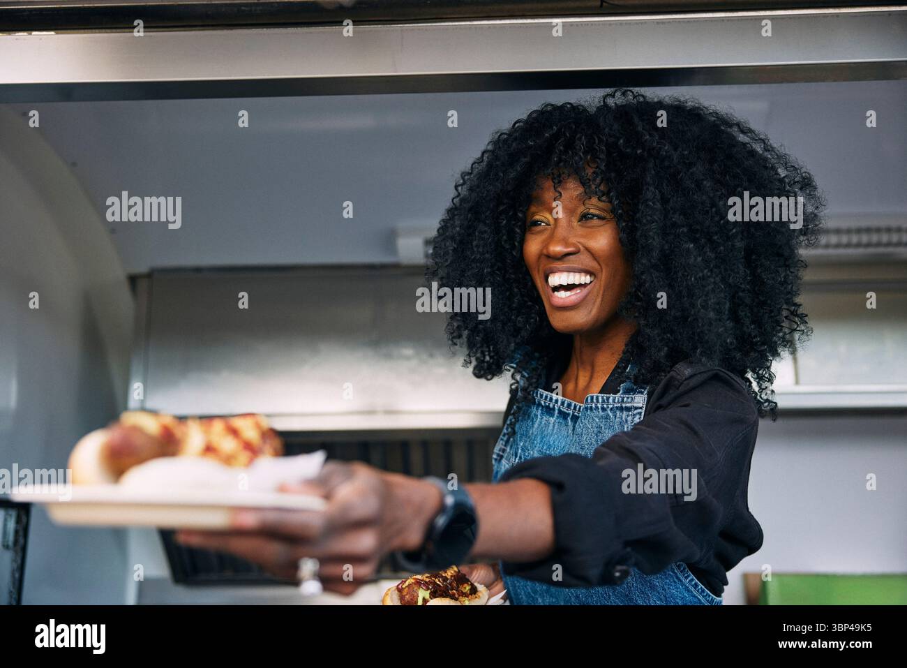 Cheerful mature female food truck owner passing out hot dog plates ...