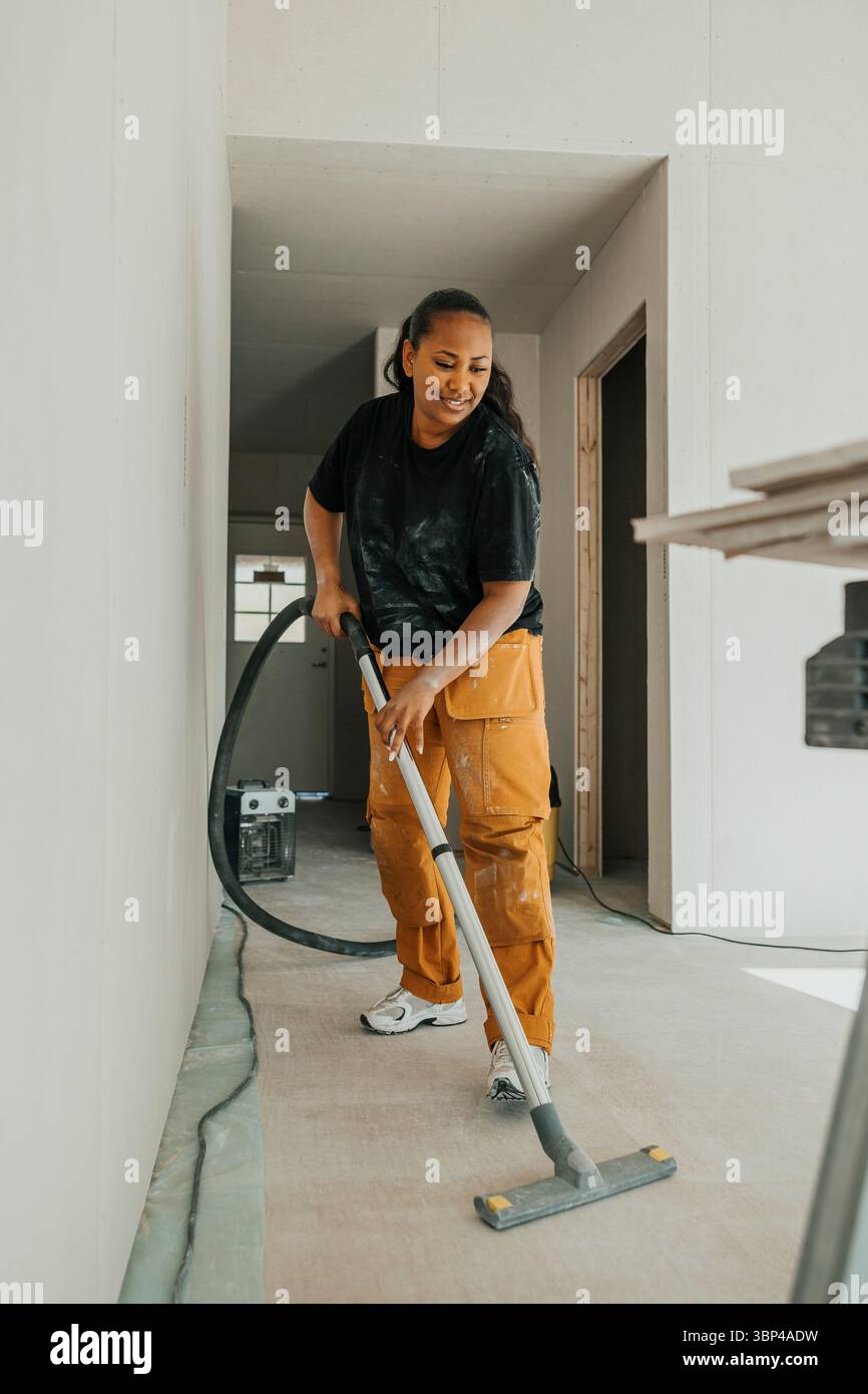 Female worker cleaning floor with vacuum cleaner at construction site ...