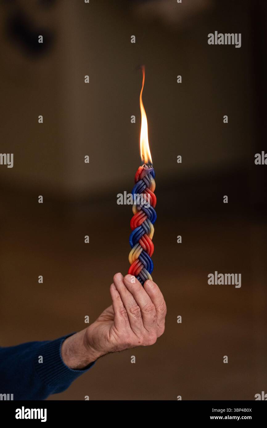 A man holds a multi-colored, braided, wax candle while reciting ...