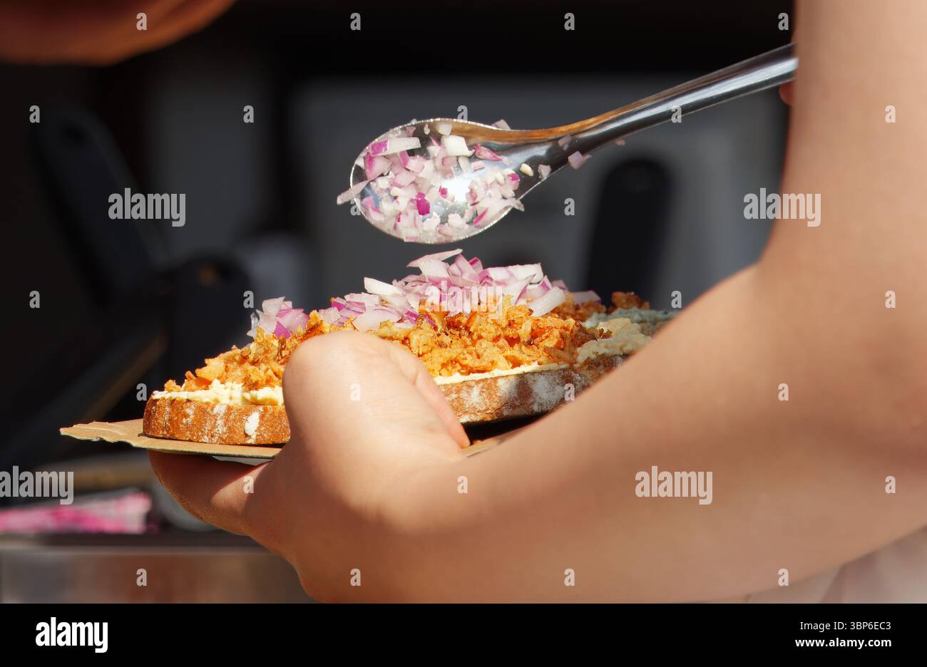 Close-up of a person garnishing an open-faced sandwich with chopped red ...