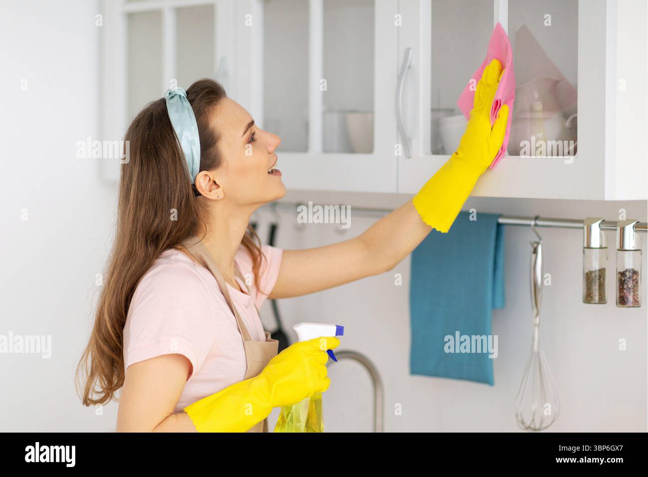 Lovely millennial housemaid wiping kitchen cabinet, performing house ...