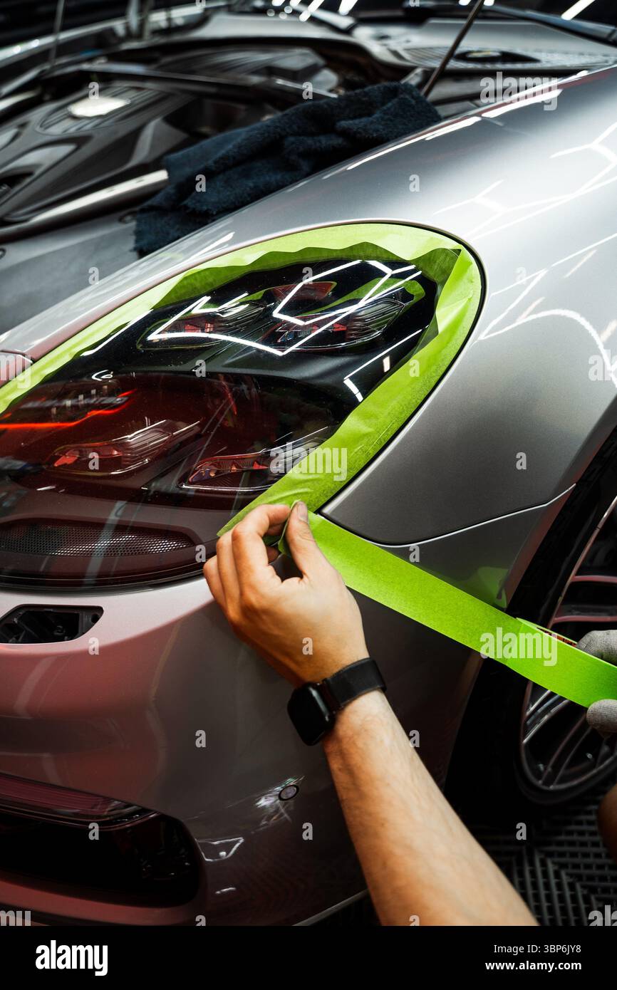 Technician applies masking tape around car panels before installing ...