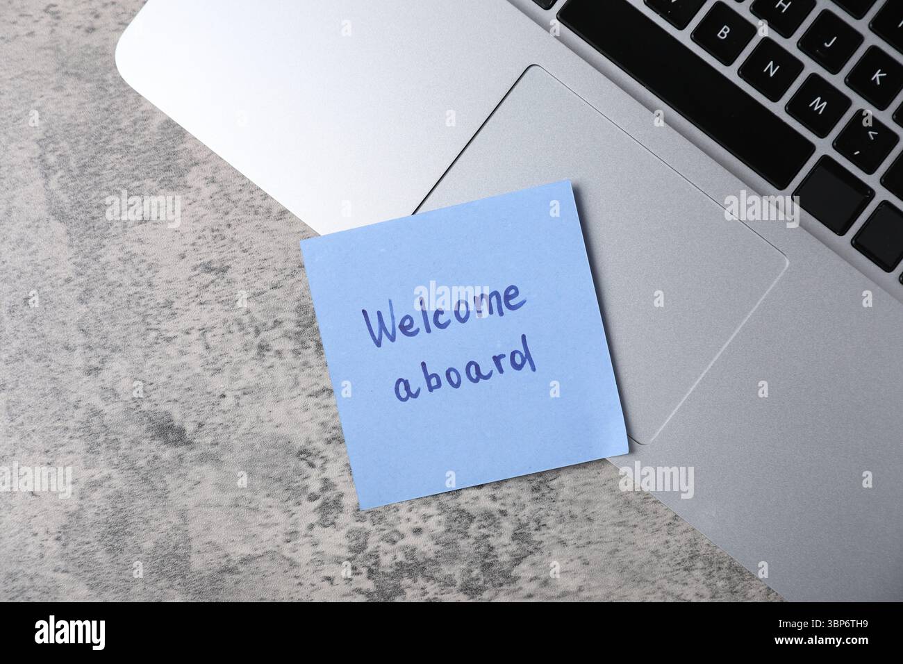 Sticky note with phrase Welcome Aboard and laptop on grey table, top ...
