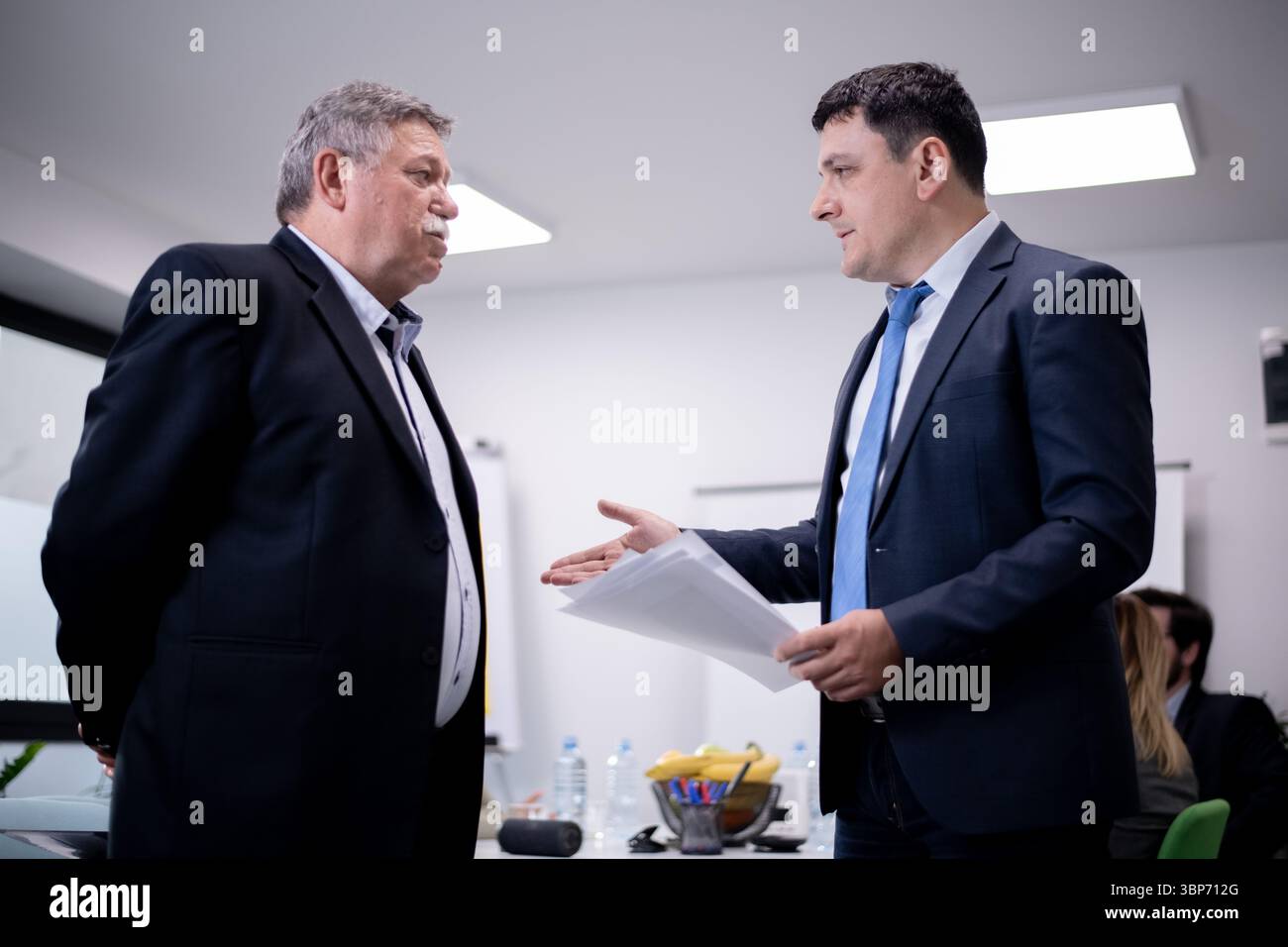 Two men in formal suits discuss documents in a professional office ...