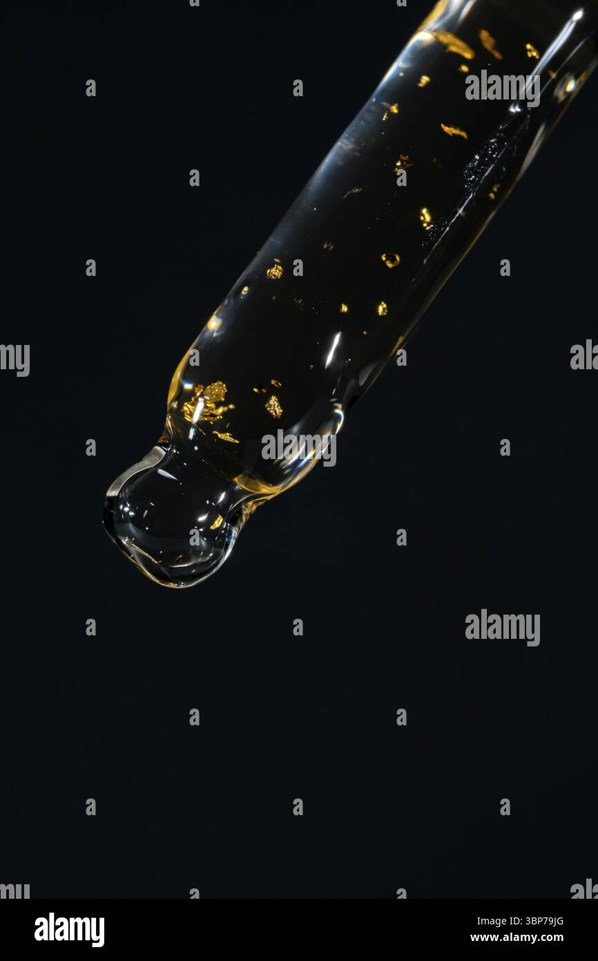 Cosmetic pipette with dripping 24k gold face serum on black background ...