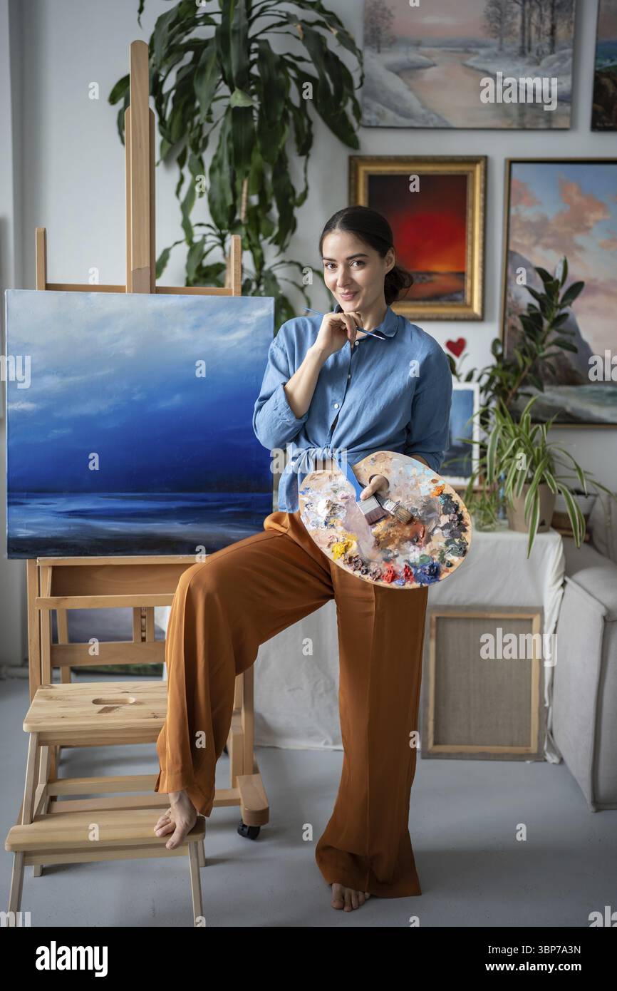 Satisfied artist woman smiling looking at camera holding colour palette ...