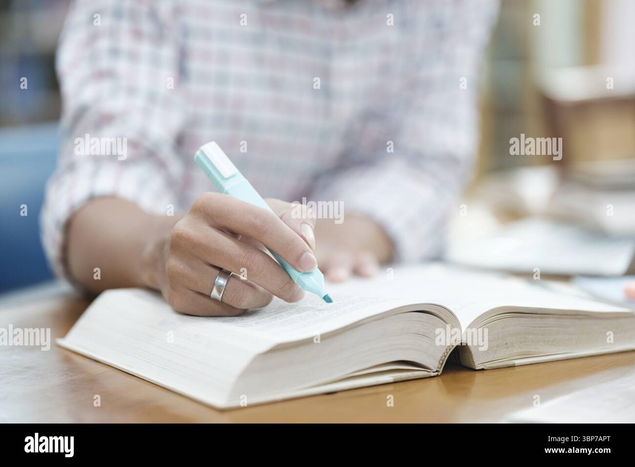 A student writes notes in a notebook while studying in a library, with ...