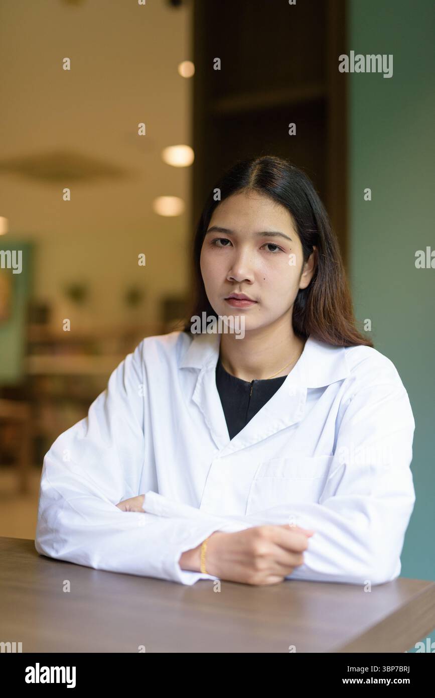 Young Asian woman doctor wearing white lab coat and stethoscope sitting hospital library ...