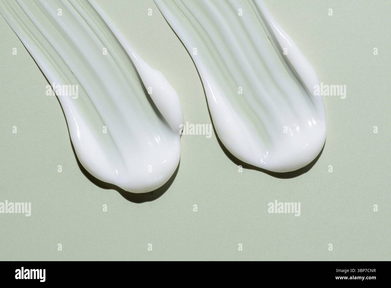 Texture of white cream on green background. Smear of moisturizer close ...