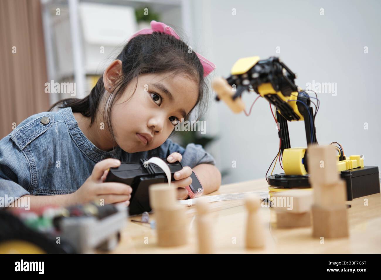 A primary school girl focuses on operating a robotic arm with a remote ...