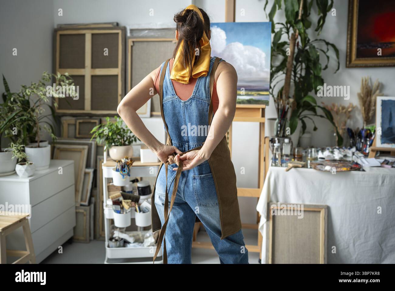 Female artist tying apron before starting work at artwork project ...