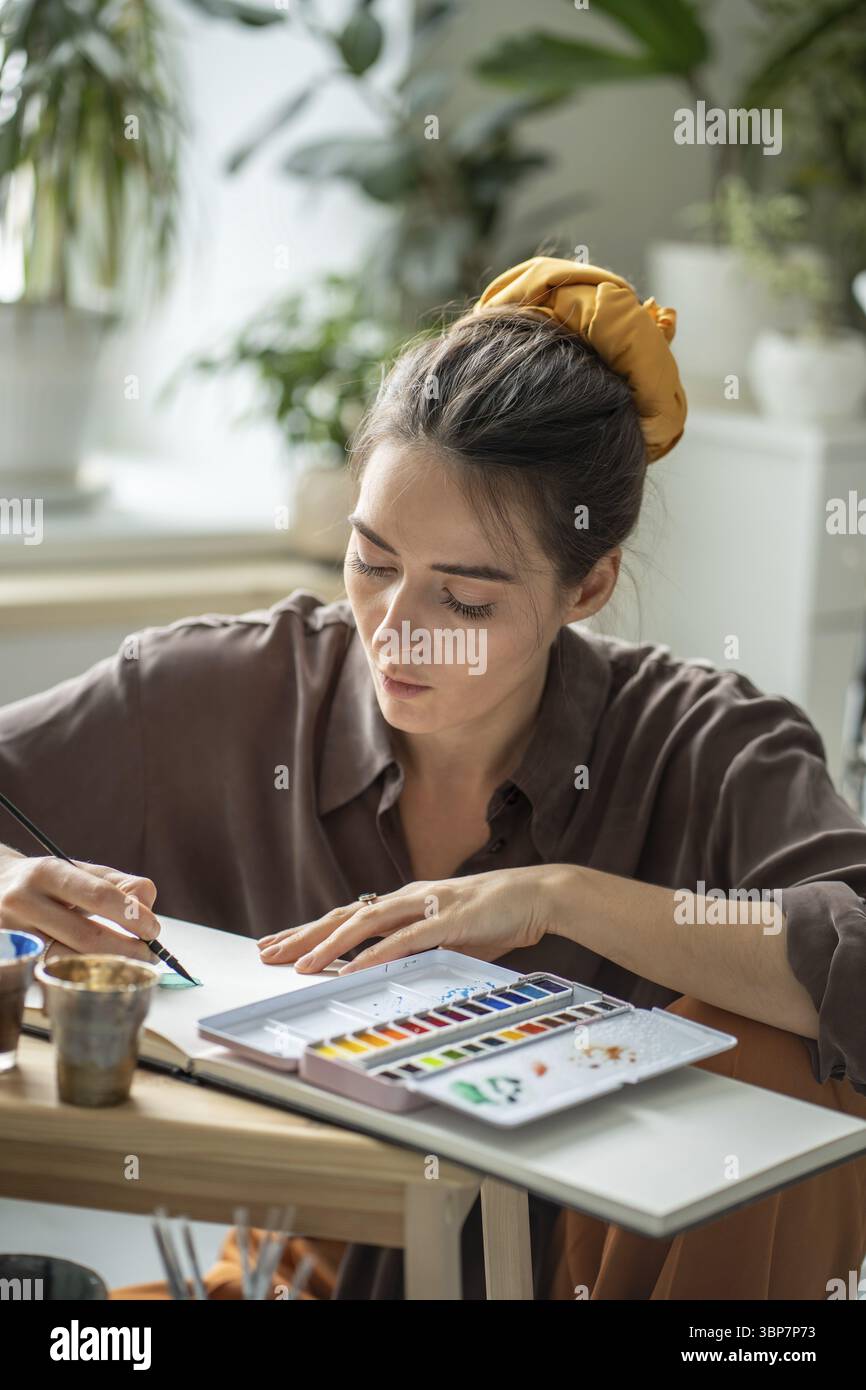 Creative concentrated woman artist painting with watercolour palette ...
