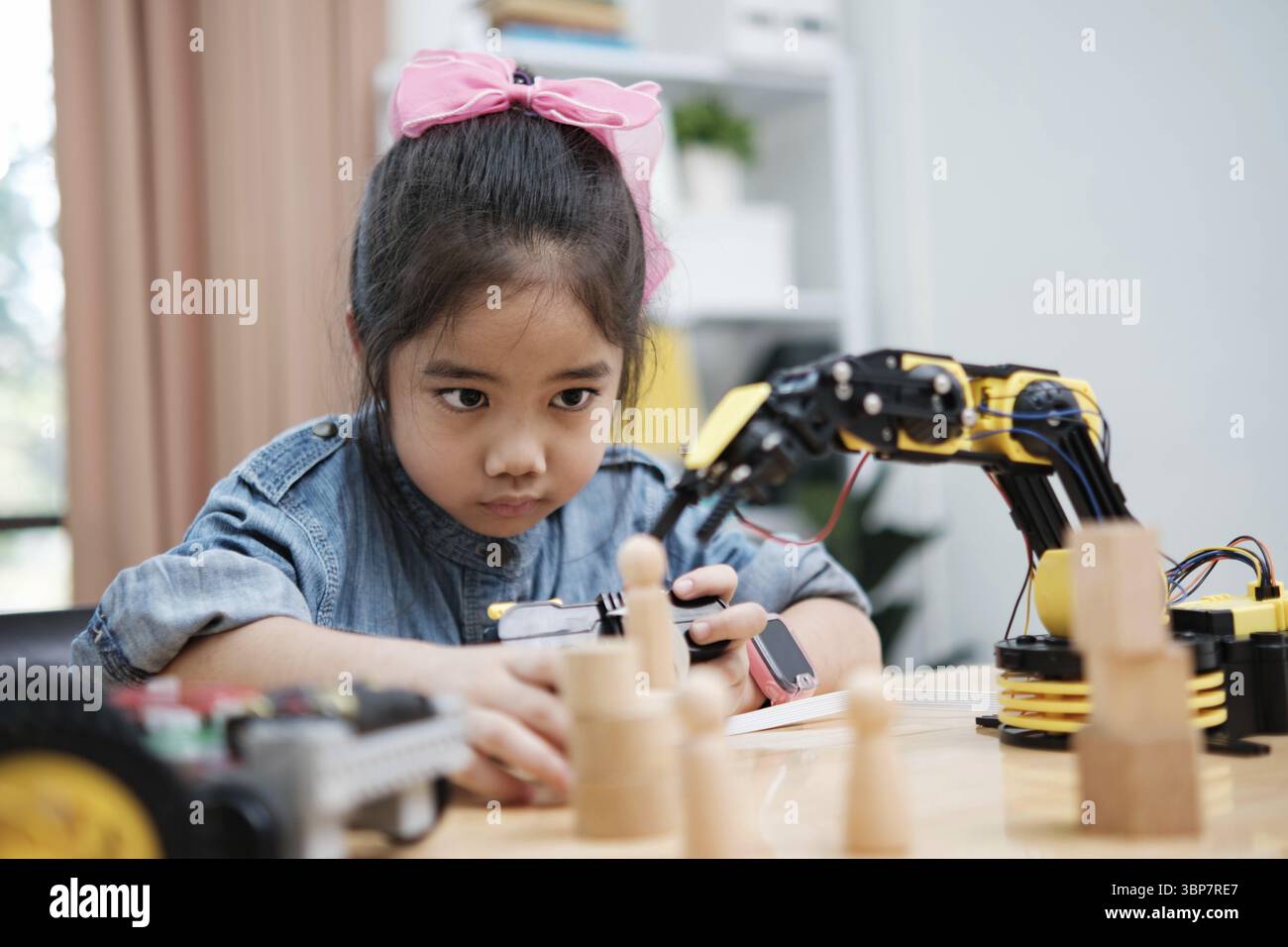 A primary school girl focuses on operating a robotic arm with a remote ...