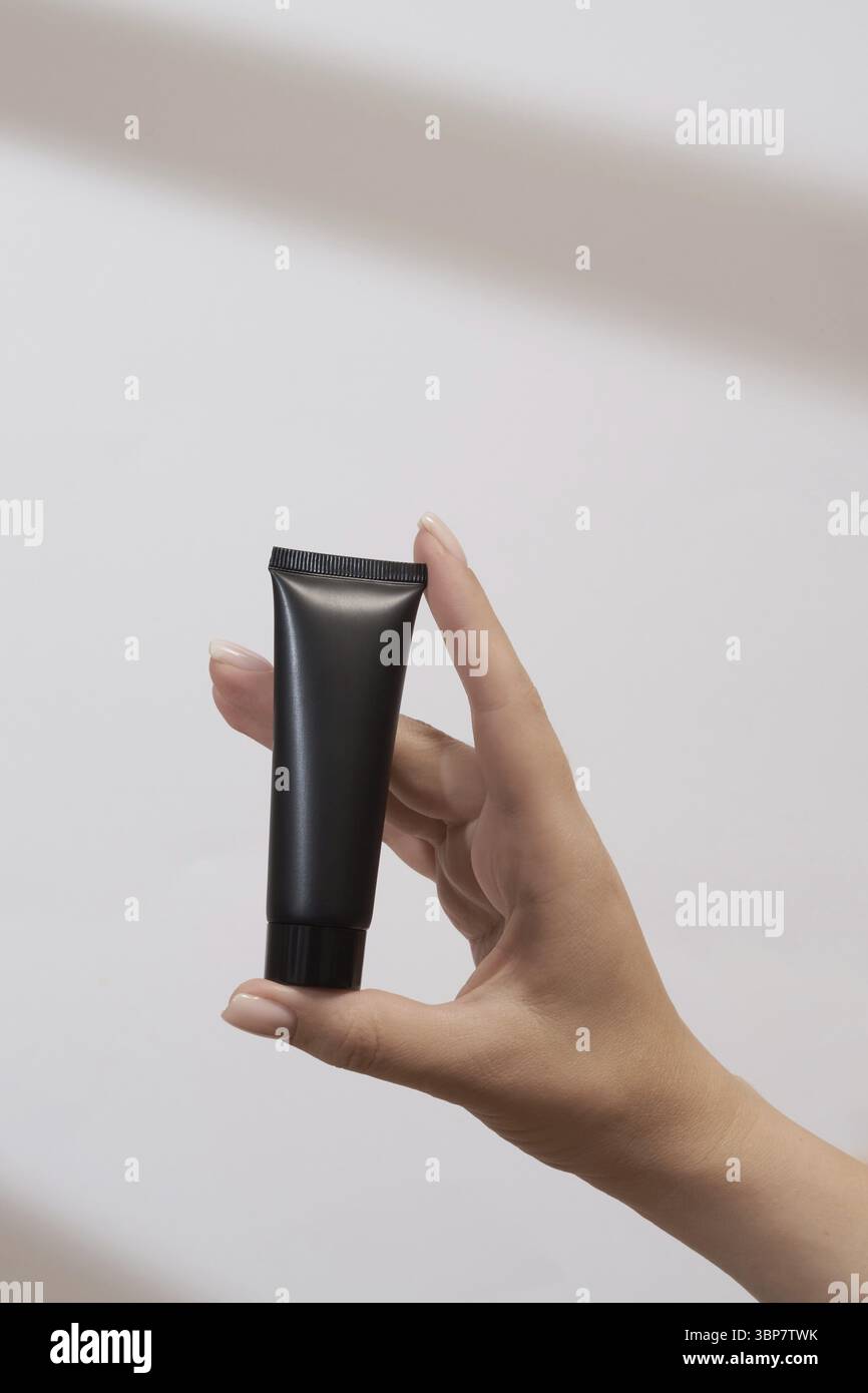 Woman's hand holds a mockup of black tube of cream. Unlabeled packaging ...
