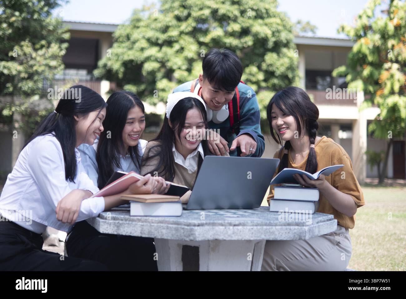 A group of college students studying together outdoors on campus, using ...
