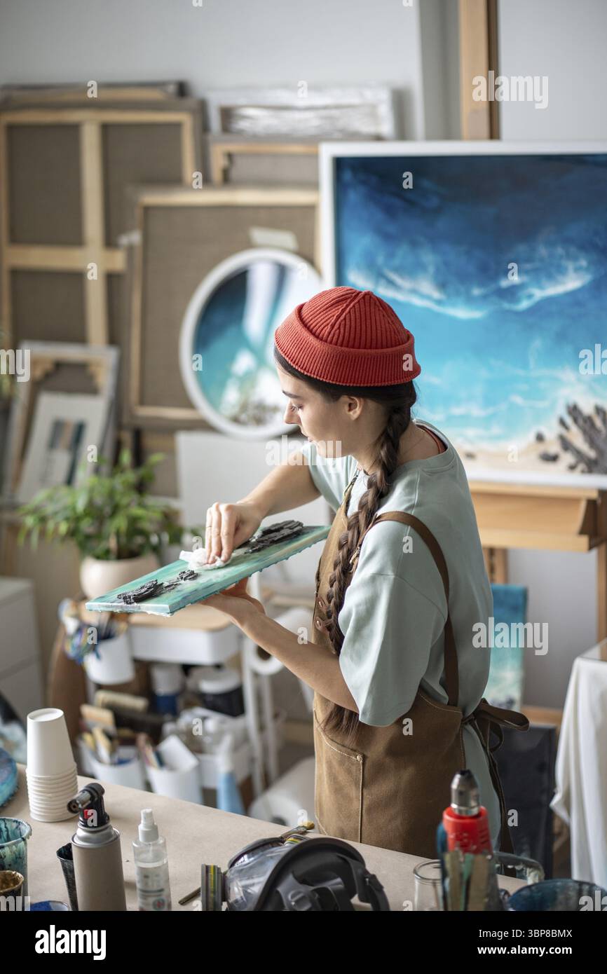 Focused creative woman artist puts final touches on piece of epoxy ...